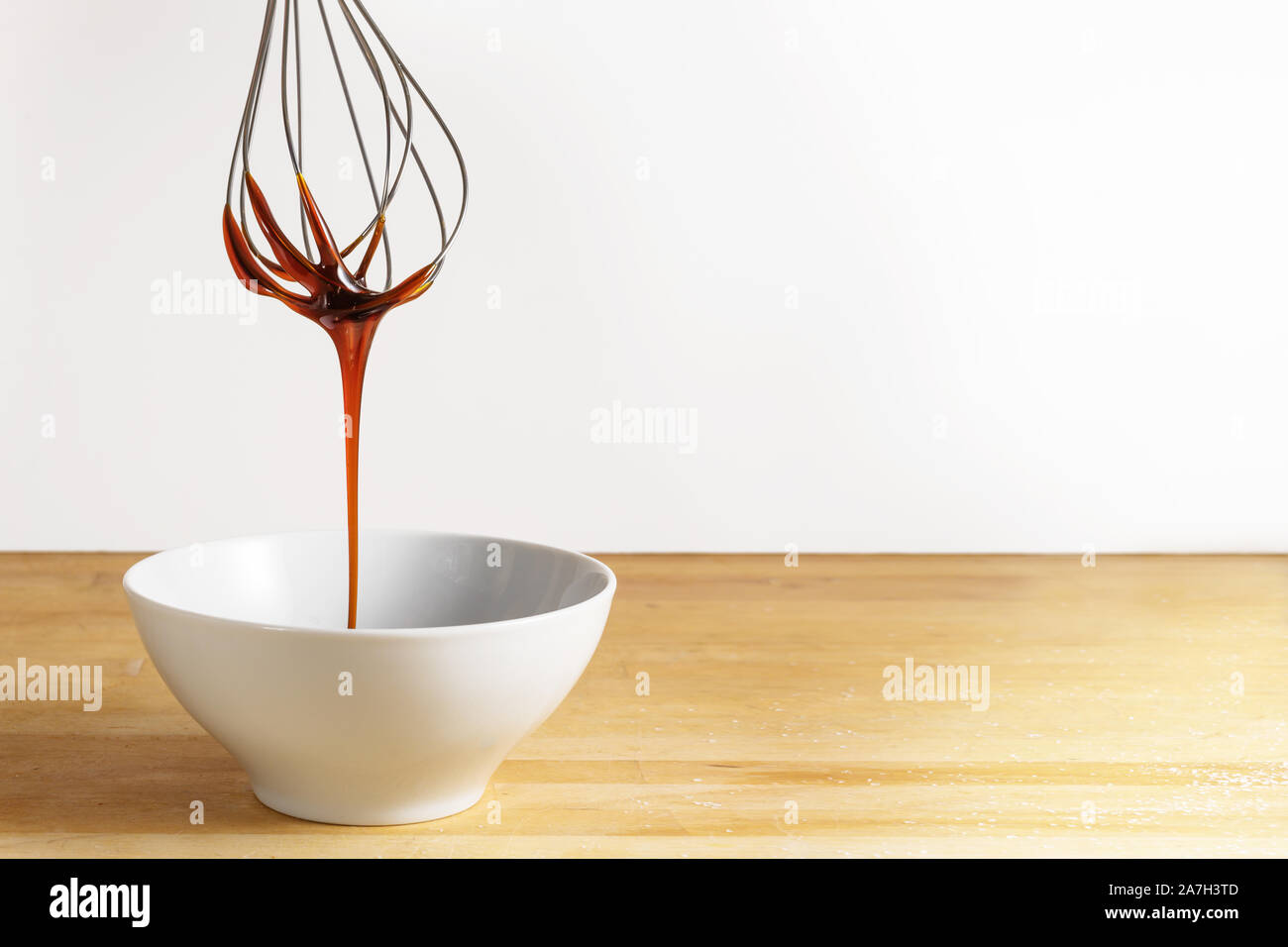Brown sugar syrup flows from a wire whisk into a white bowl, wooden ...