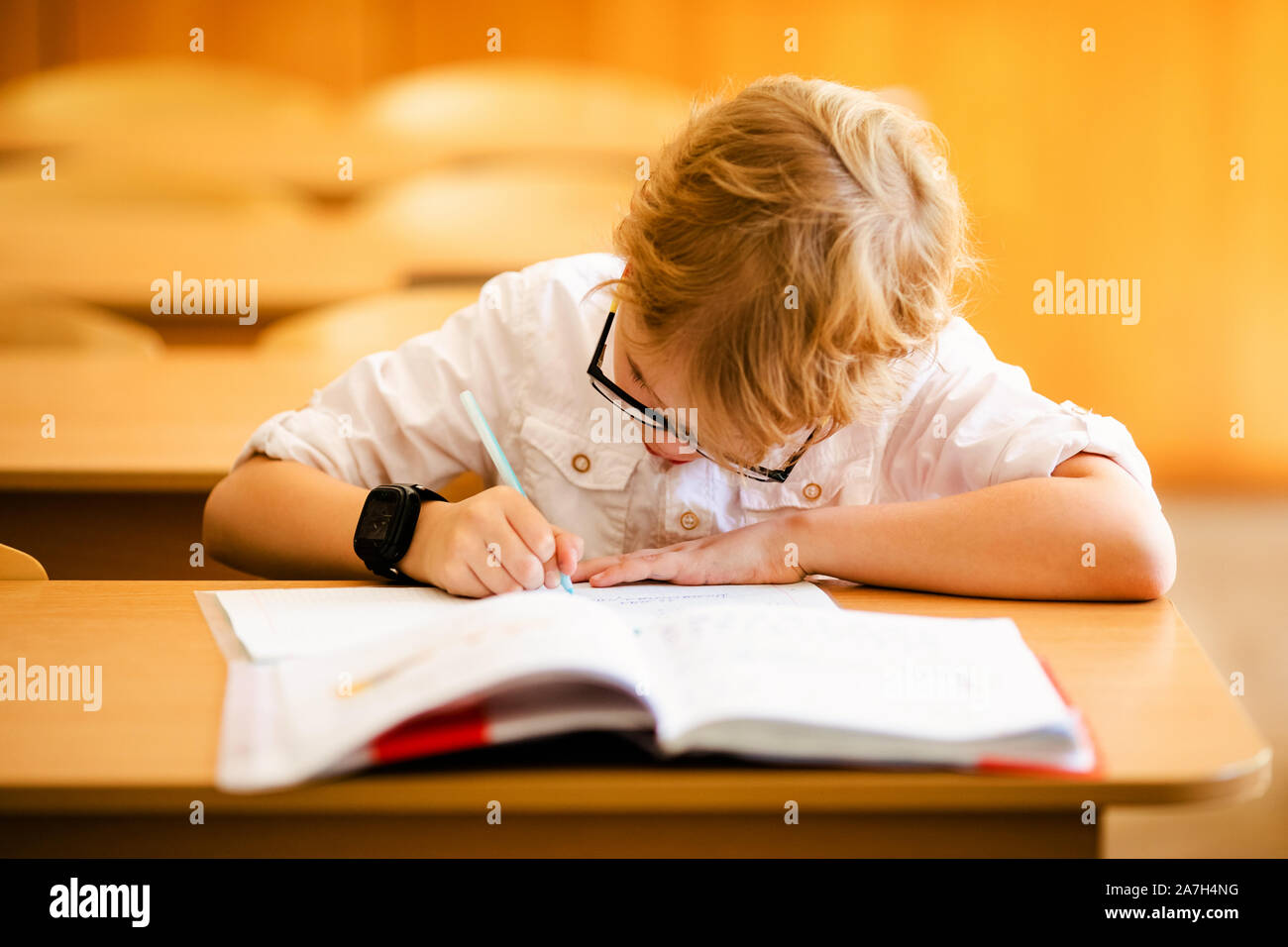 Seven years old child with glasses writing his homework at school. Boy ...