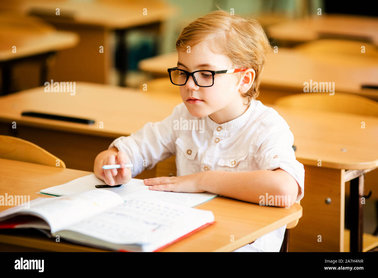 Seven years old child with glasses writing his homework at school. Boy ...