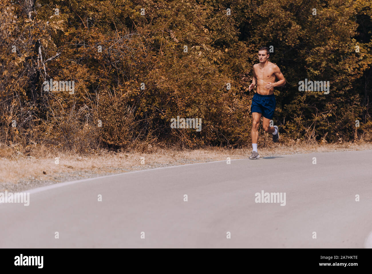 Healthy shirtless man running on mountain road. Rear view of athlete ...