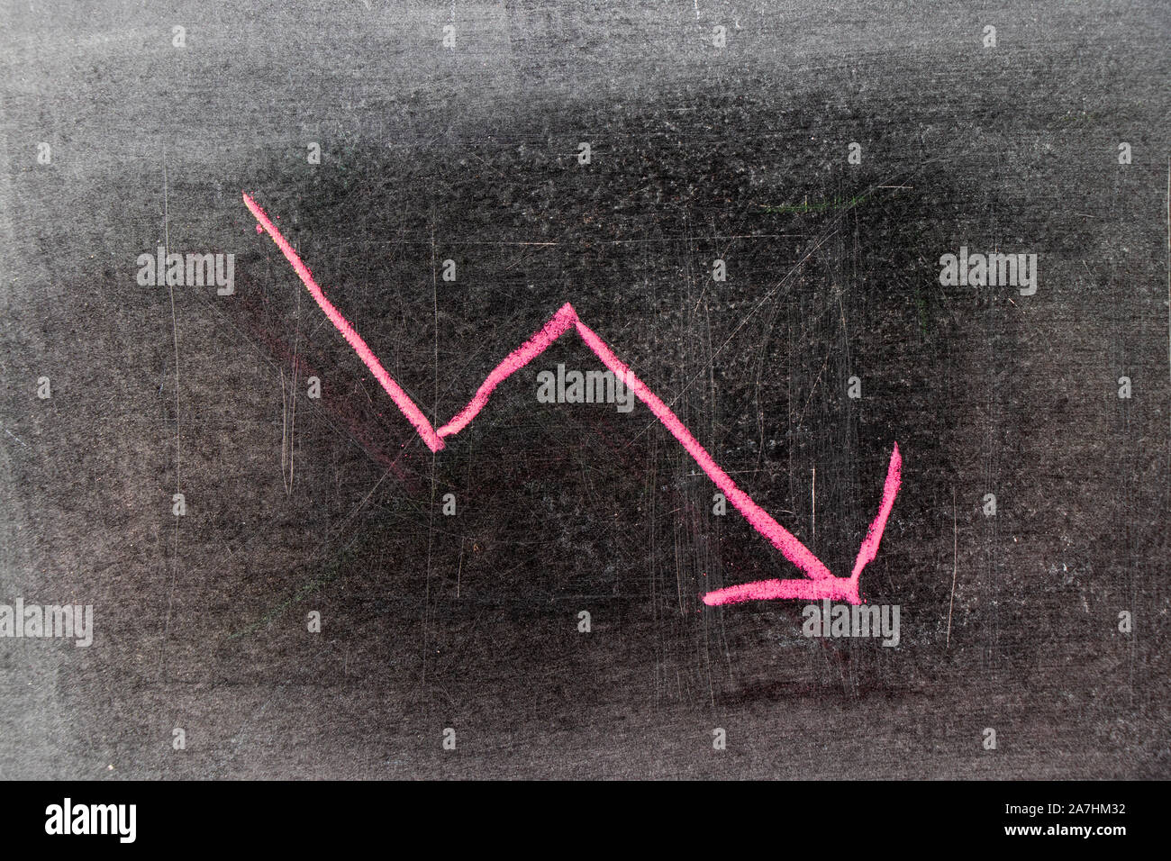 Red chalk drawing in down trend arrow shape on black board background ...