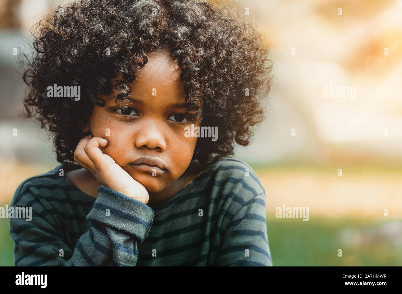 Unhappy bored little african american kid sitting in the park. The boy ...