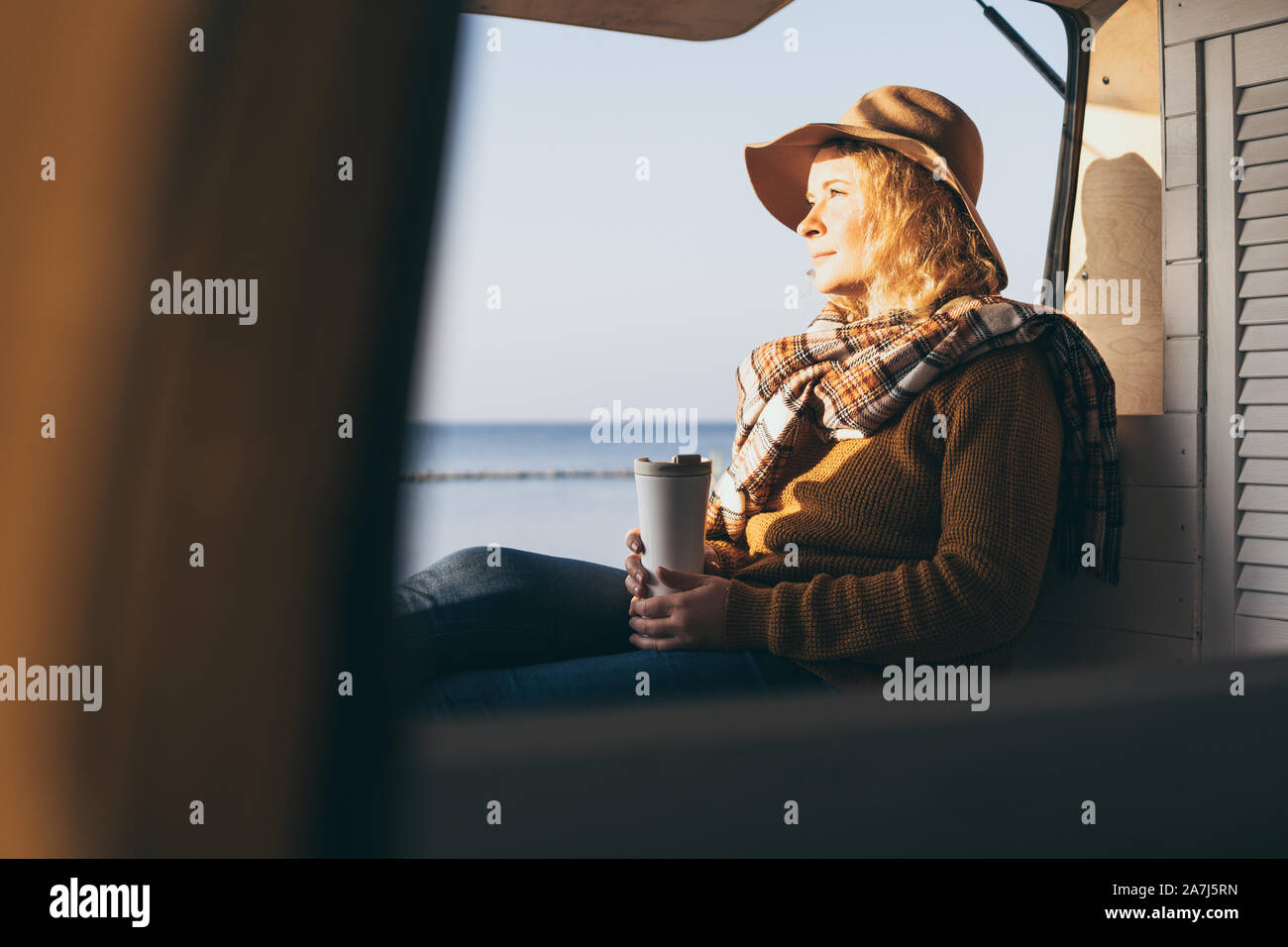 Young blonde Caucasian woman relaxing in her camper van during sunset ...