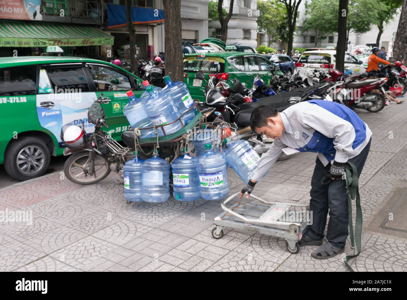 Young Vietnamese man unloading large plastic water bottles from scooter ...