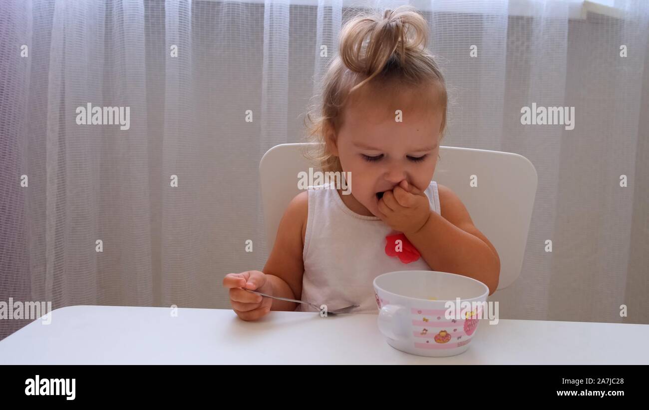 Infant girl eating baby food at a small childrens table on a white ...