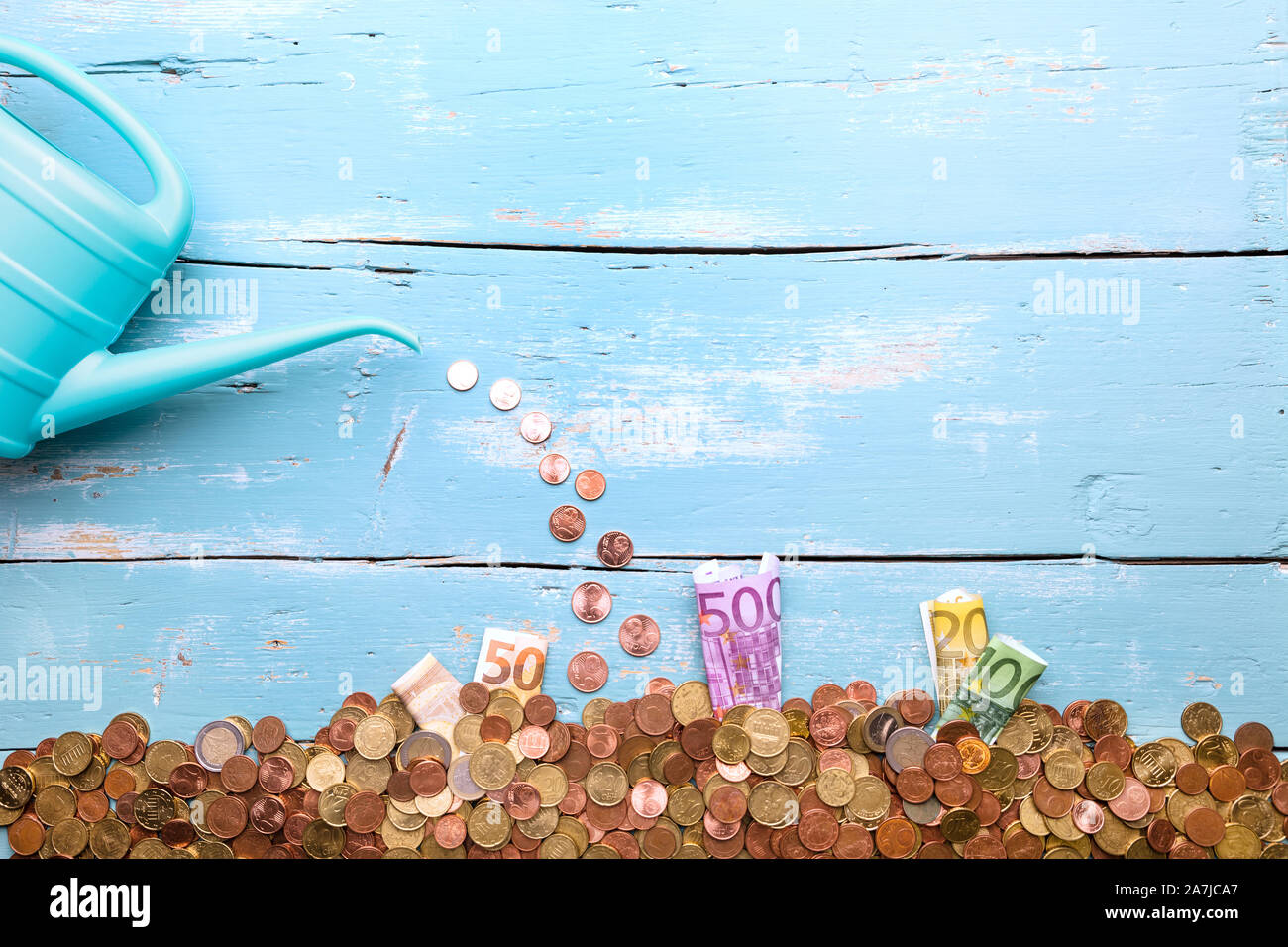 Watering can with euro coins and banknotes on blue background, concept ...