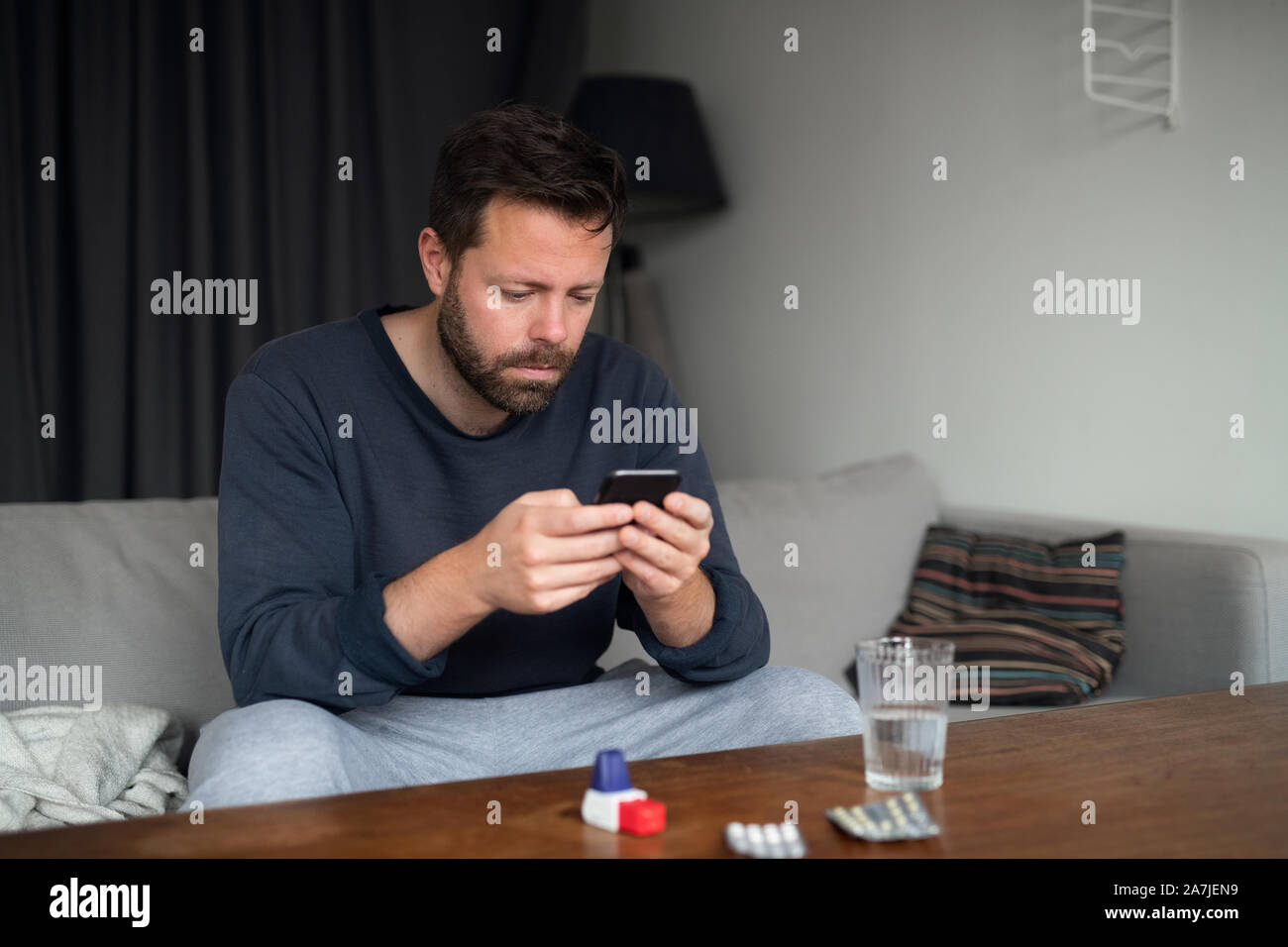 Man looking at phone after taking medicine while sick Stock Photo - Alamy