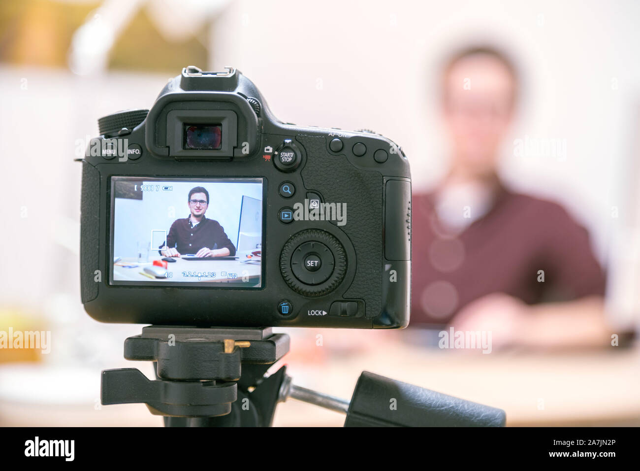 Camera on a tripod filming a blogger at home sitting on his workspace ...