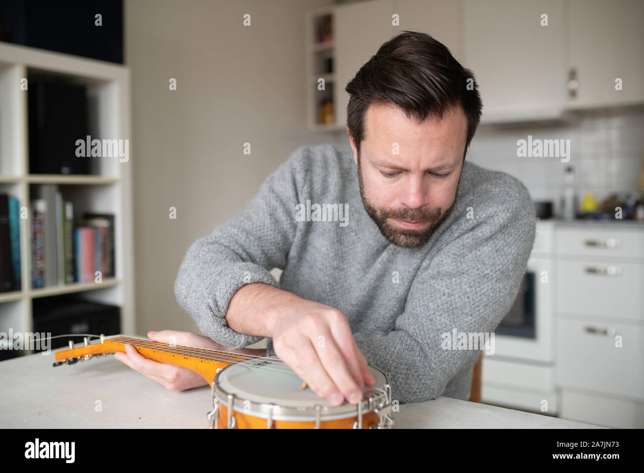 man replacing strings on banjo ukulele Stock Photo - Alamy