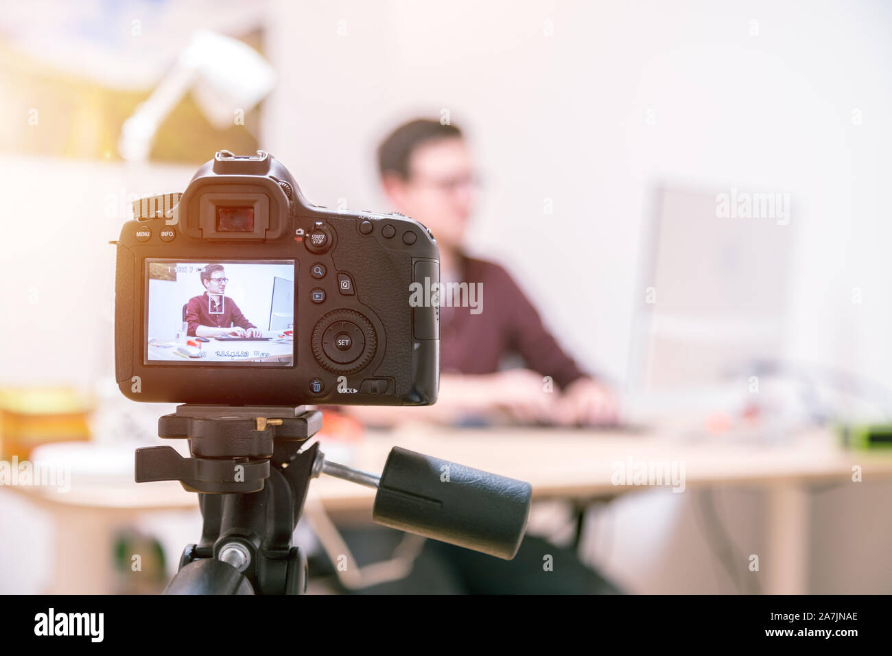Camera on a tripod filming a blogger at home sitting on his workspace ...