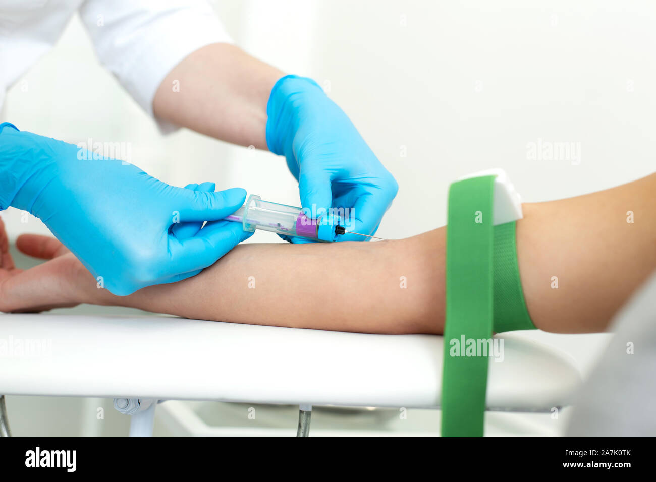 a gloved nurse inserts a needle into a vein on the patient’s arm and ...