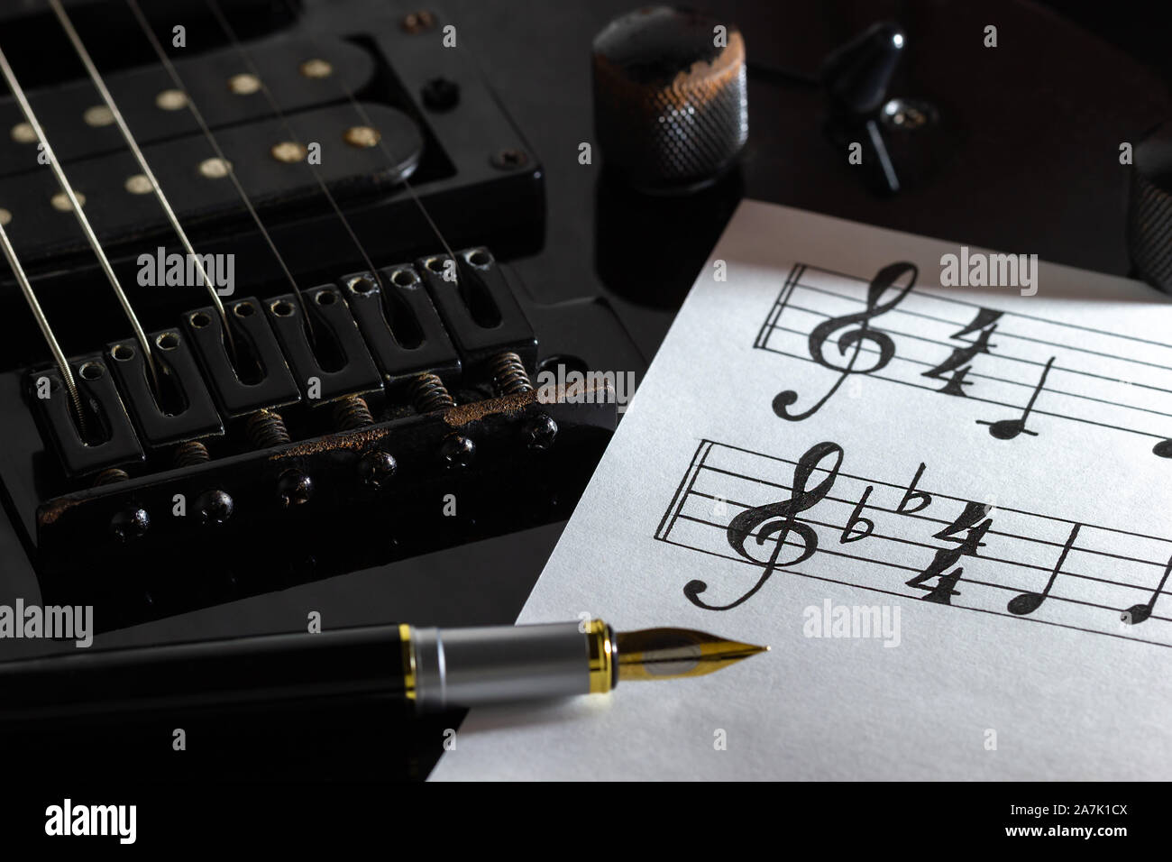 Music note and vintage pen on black electric guitar in darkness ...