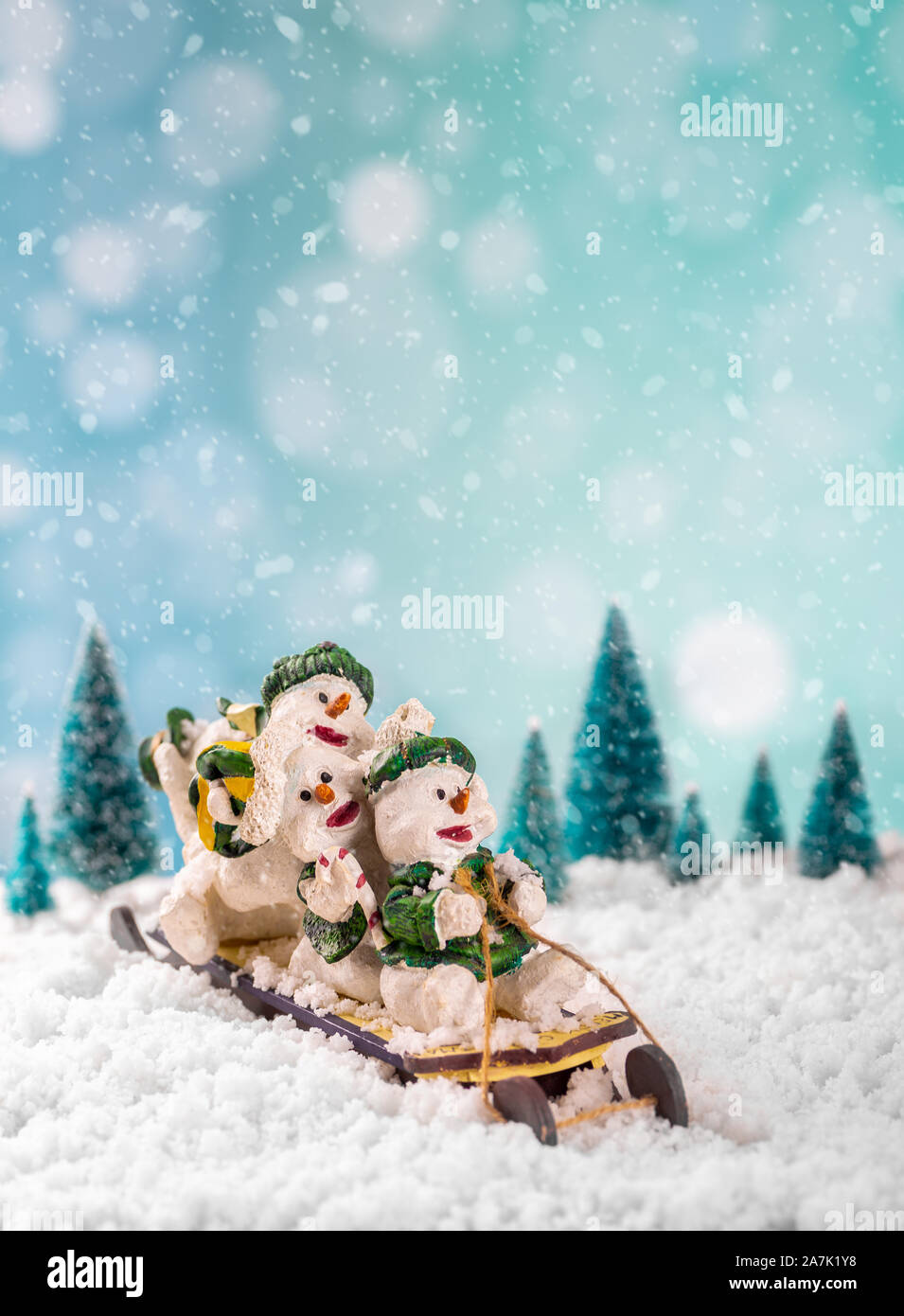 Winter scene of snowmen figurines on a sled with falling snow on a ...