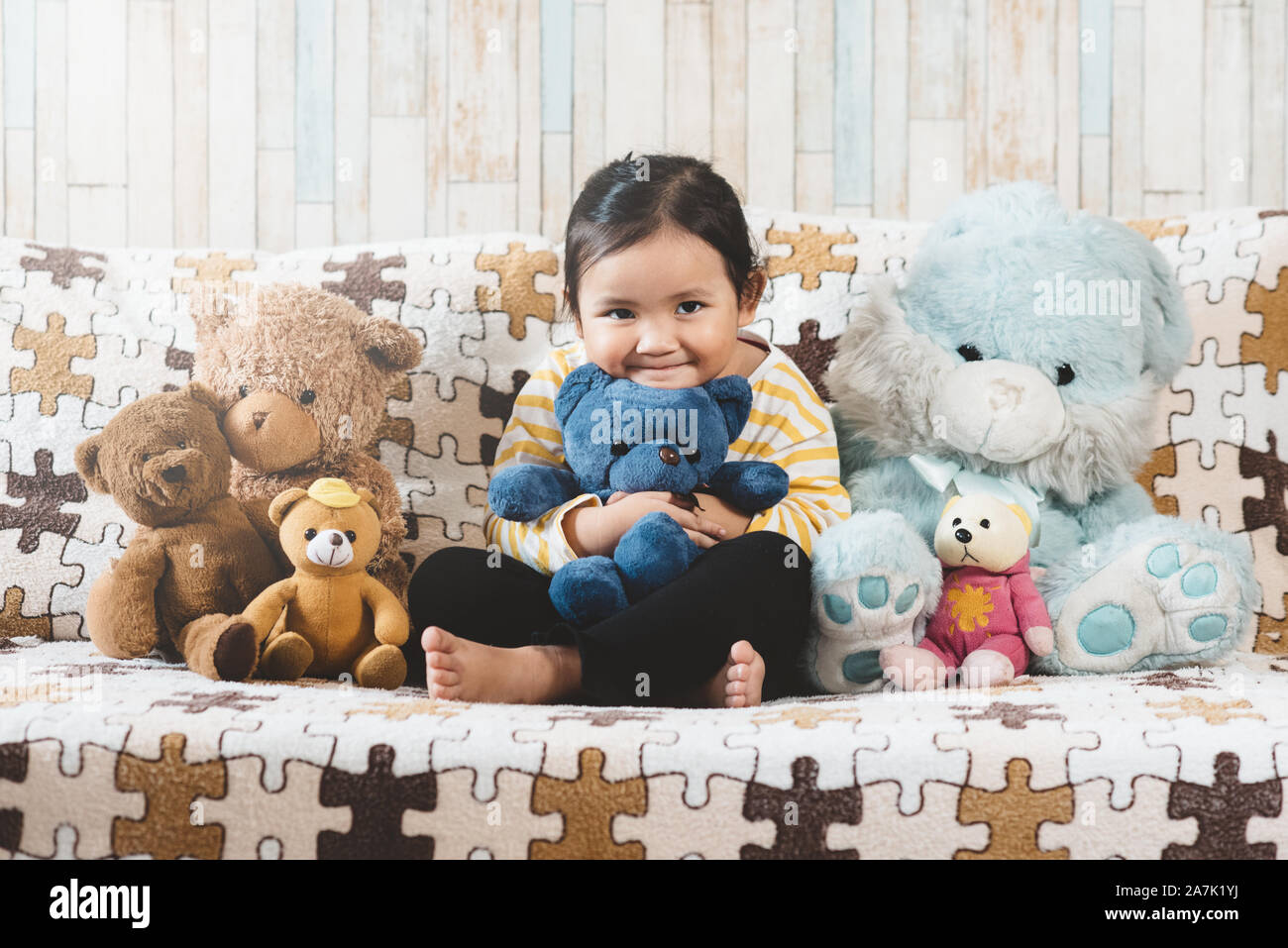 Cute little asian girl hugging her plush toy teddy bear on a sofa ...