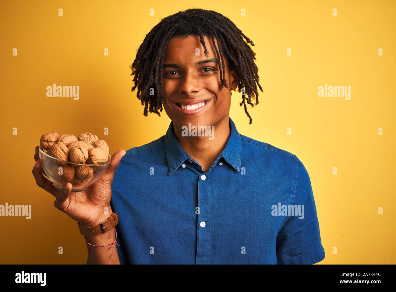 Afro american man with dreadlocks eating walnuts over isolated yellow ...