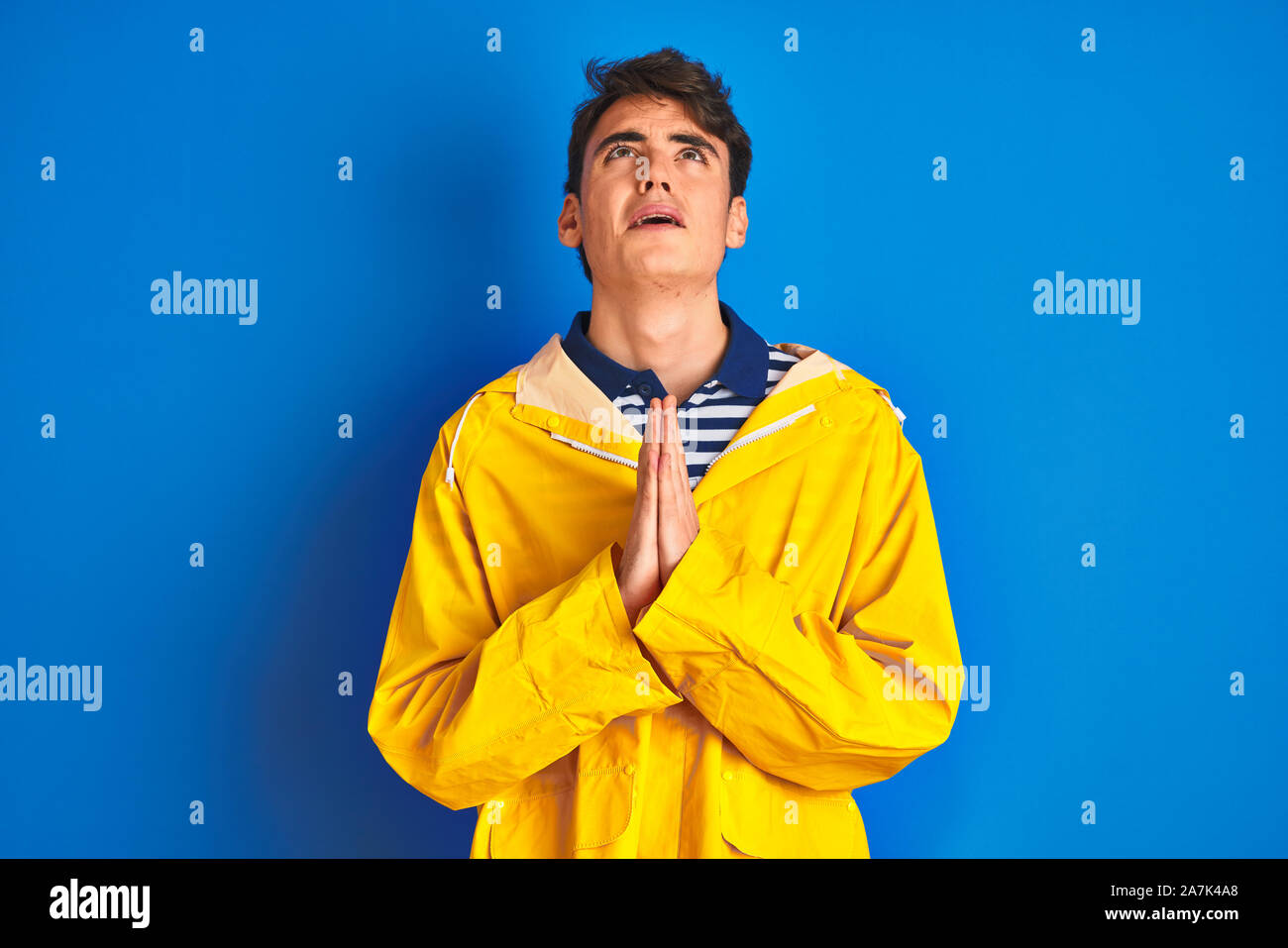 Teenager fisherman boy wearing yellow raincoat over isolated background ...