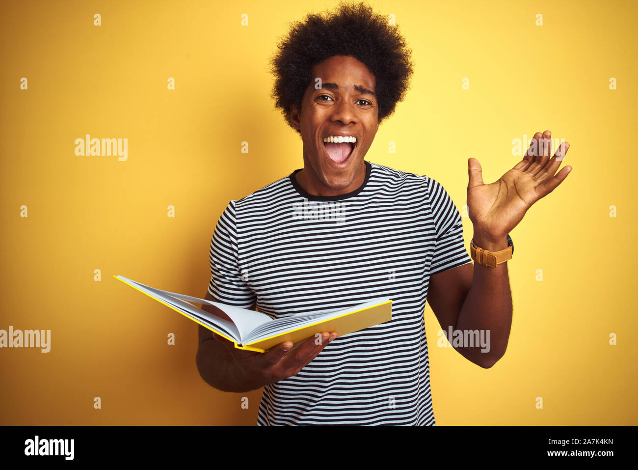 Afro american student man reading book standing over isolated yellow ...