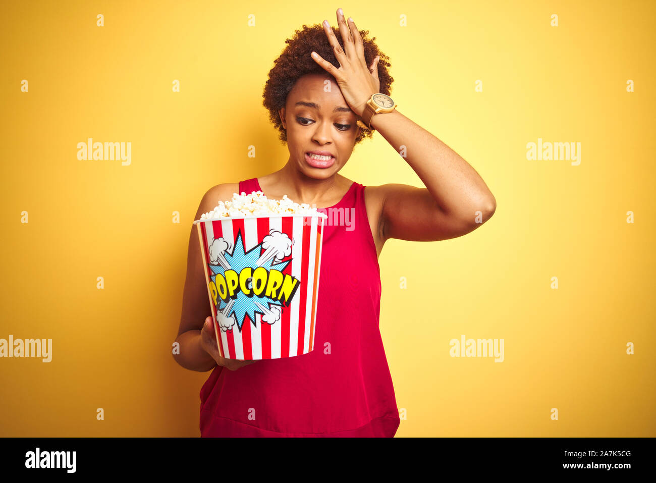 African american woman holding pack of popcorn over yellow isolated ...