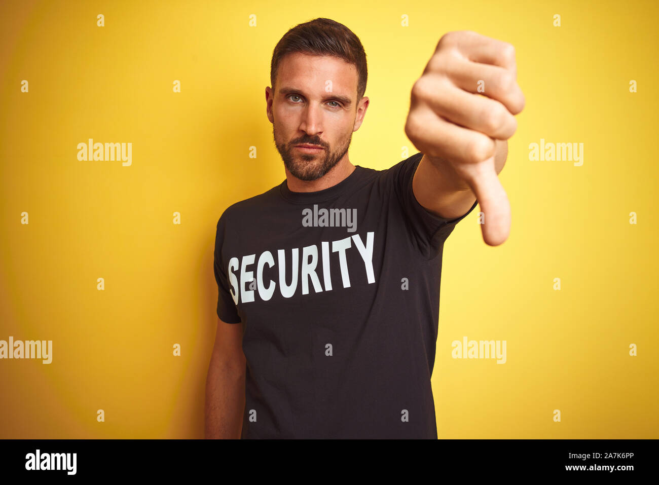 Young safeguard man wearing security uniform over yellow isolated ...