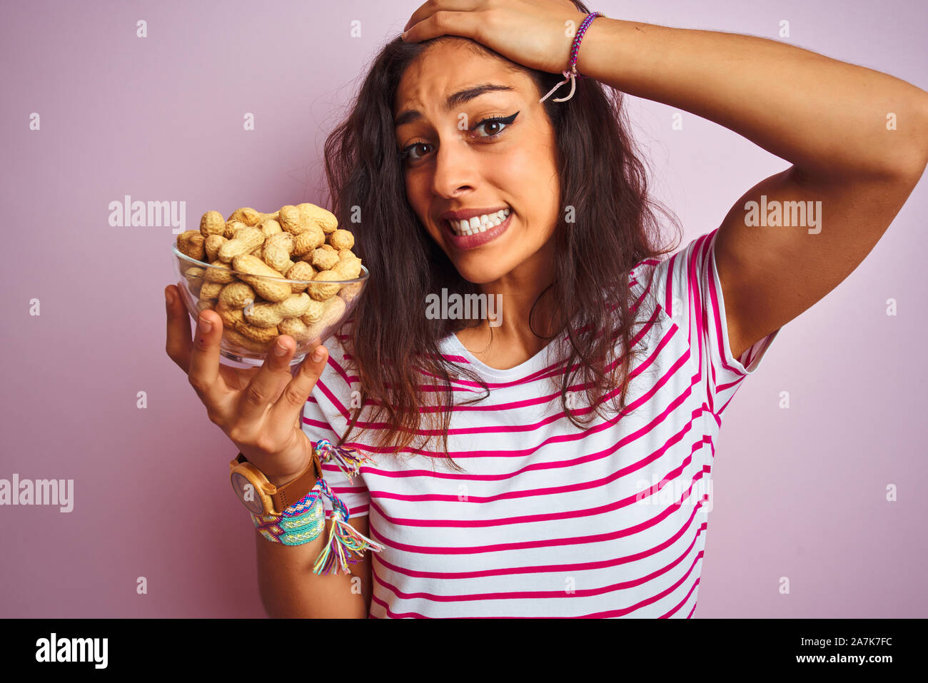 Young beautiful woman holding bowl with peanuts over isolated pink ...