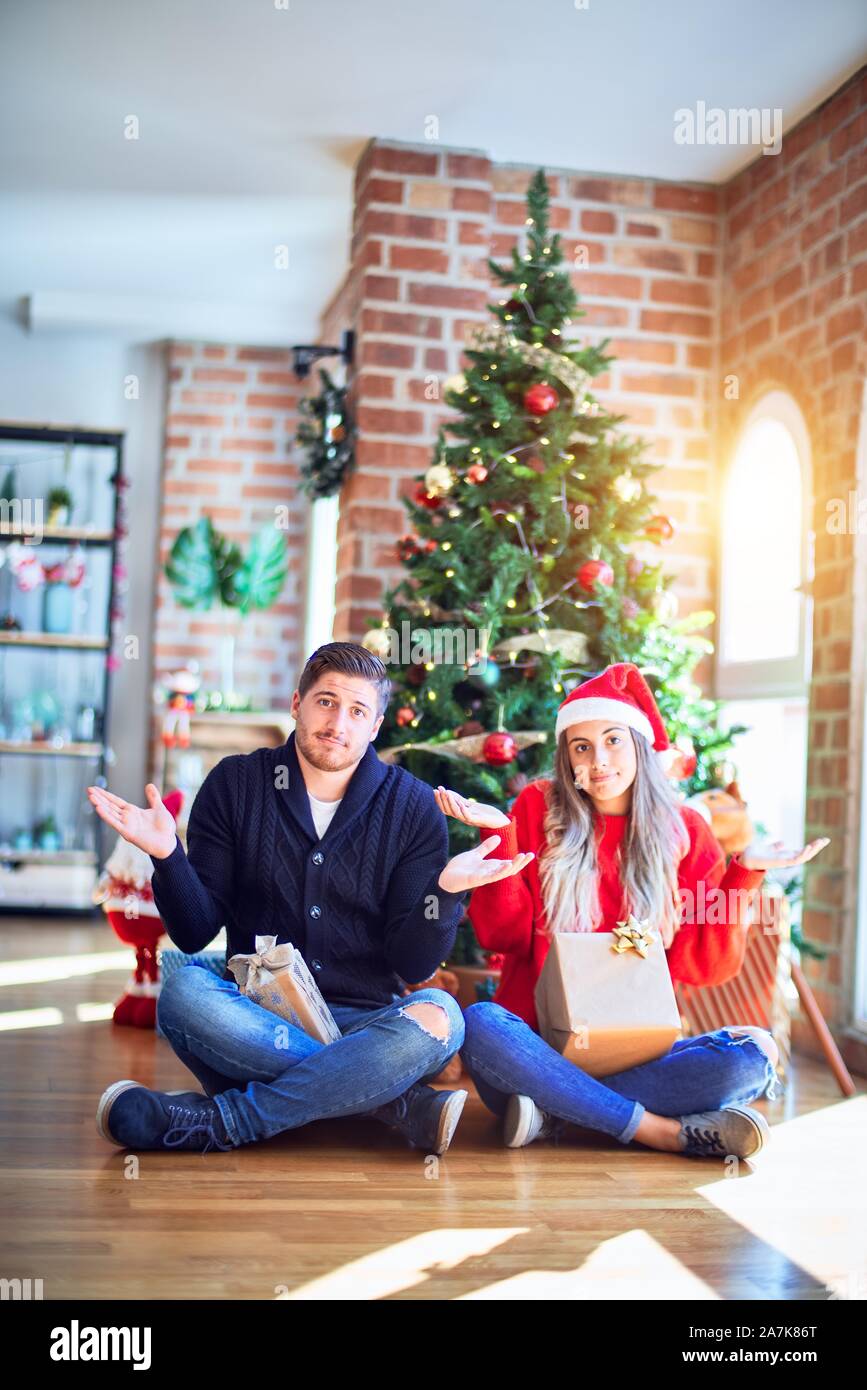Young couple wearing santa claus hat sitting on the floor around ...