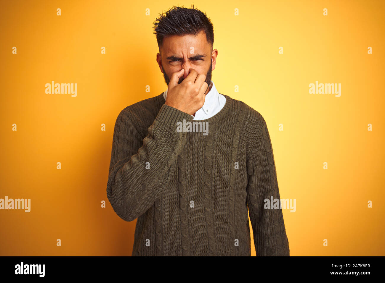 Young indian man wearing green sweater and shirt standing over isolated ...
