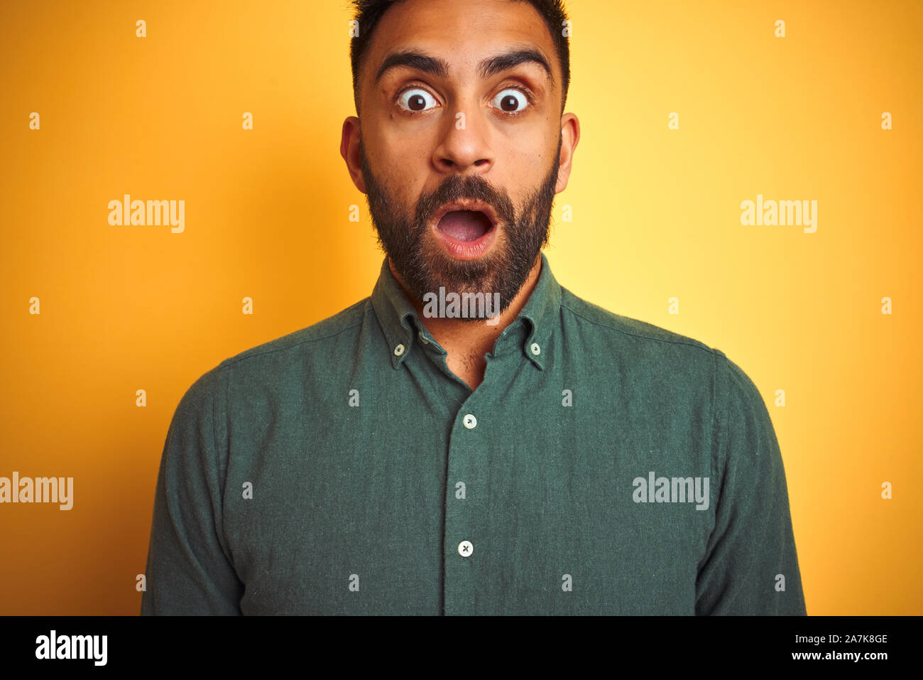 Young indian man wearing green shirt standing over isolated yellow ...