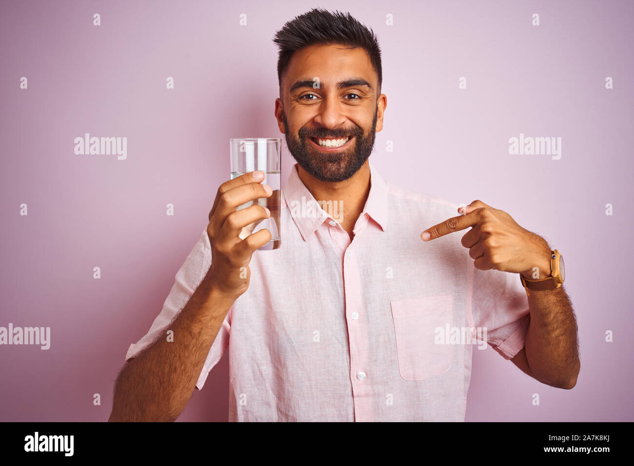 Young handsome indian man dinking glass of water over isolated pink ...