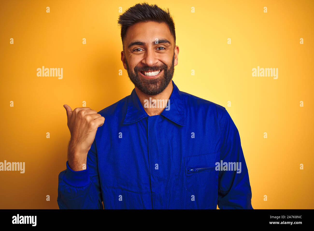 Handsome indian worker man wearing uniform over isolated yellow ...