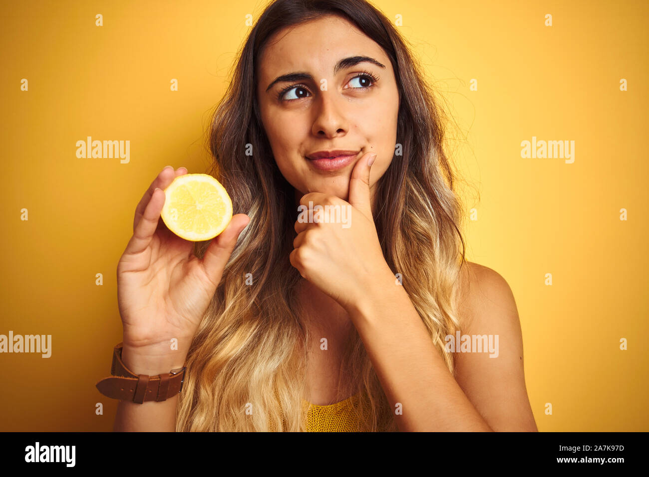 Young beautiful woman holding half lemon over yellow isolated ...