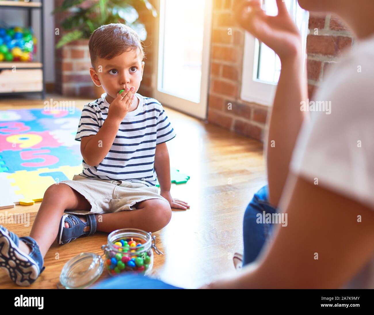 Beautiful teacher and toddler boy sitting eating small chocolate balls ...