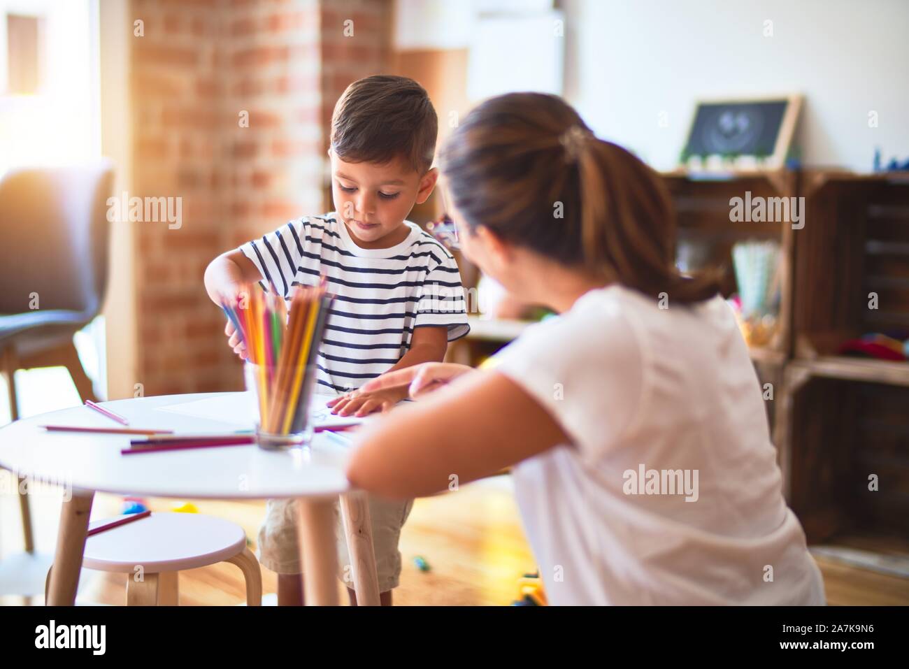 Beautiful teacher and toddler boy drawing draw using colored pencils at ...