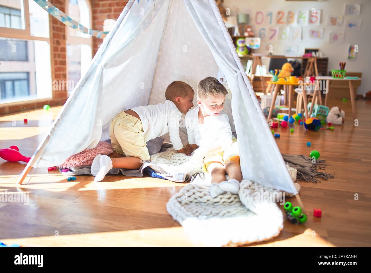 Adorable blonde twins playing inside tipi around lots of toys at ...