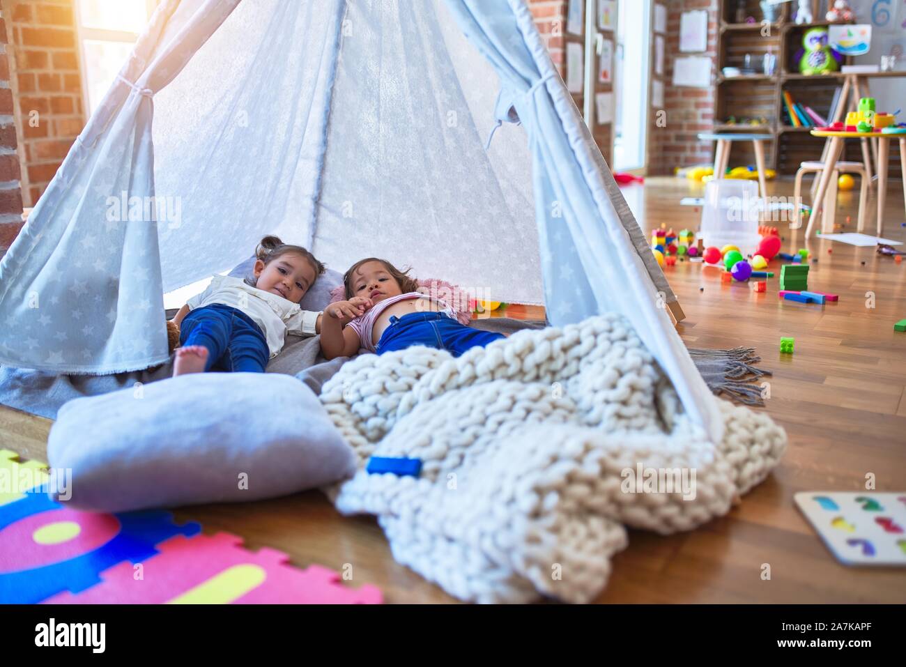Adorable toddlers lying down over blanket inside tipi smiling at ...