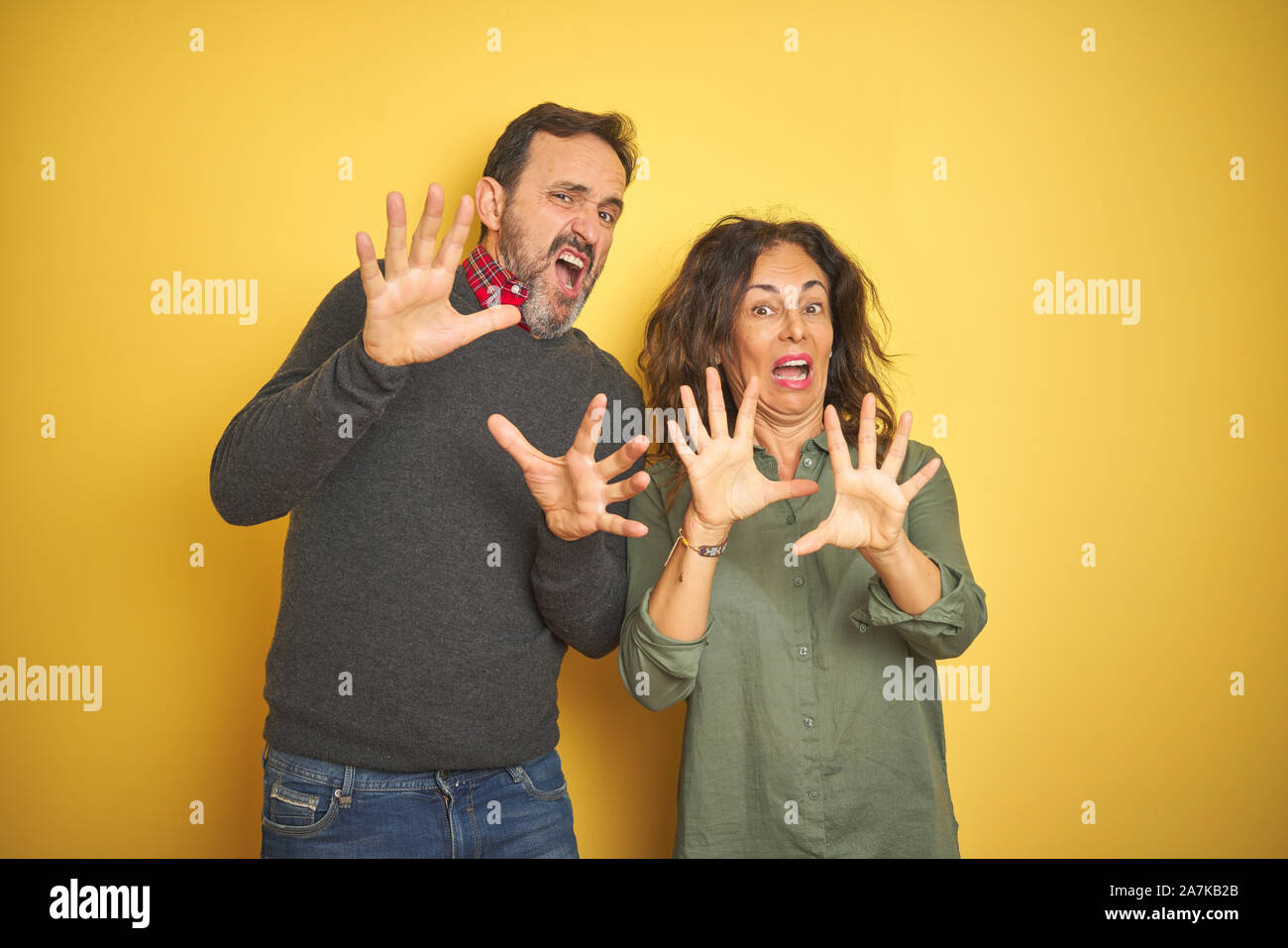 Beautiful middle age couple over isolated yellow background afraid and ...