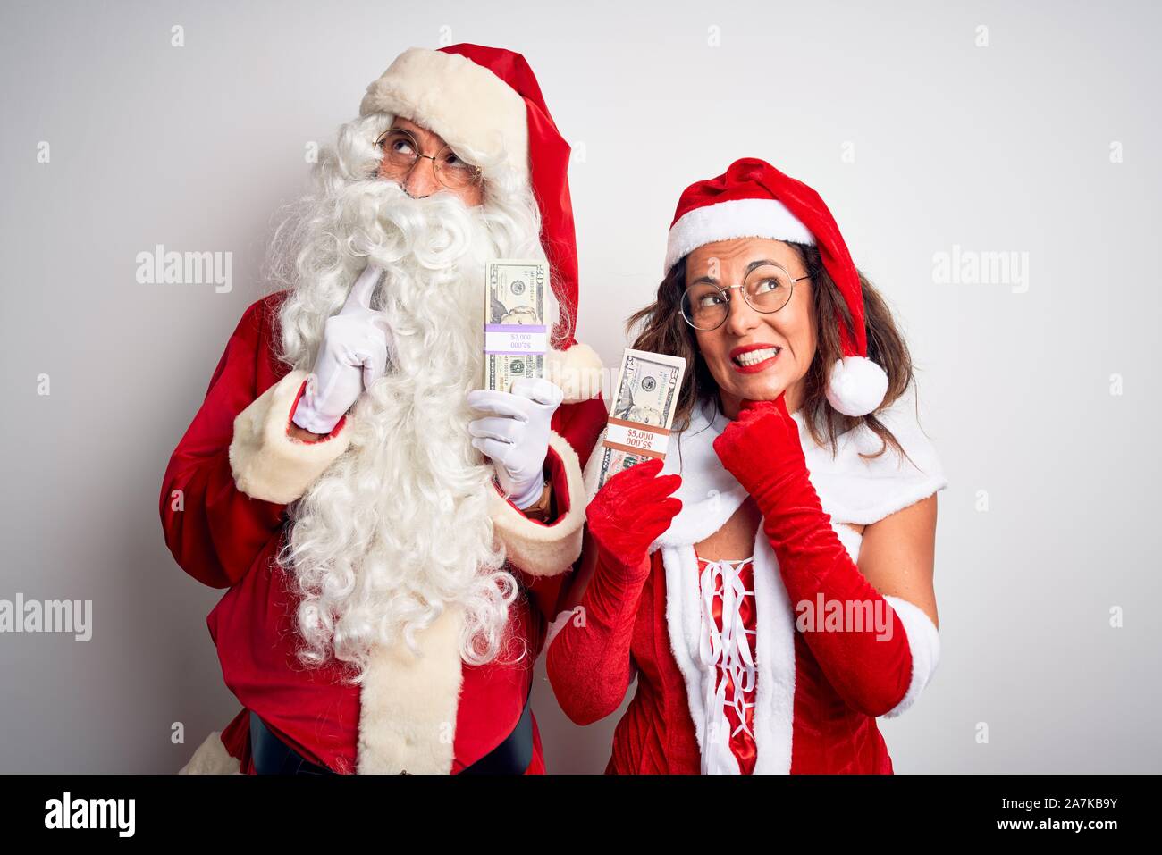 Senior couple wearing Santa Claus costume holding dollars over isolated ...