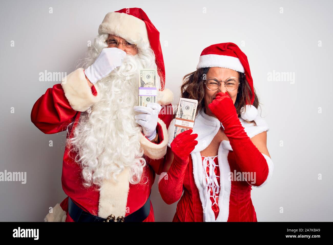 Senior couple wearing Santa Claus costume holding dollars over isolated ...