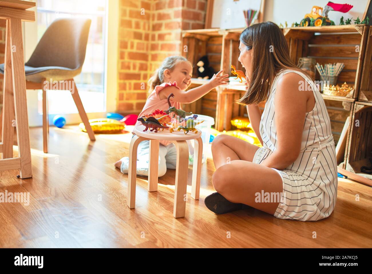 Beautiful teacher and blond student toddler girl playing with dinosaurs ...