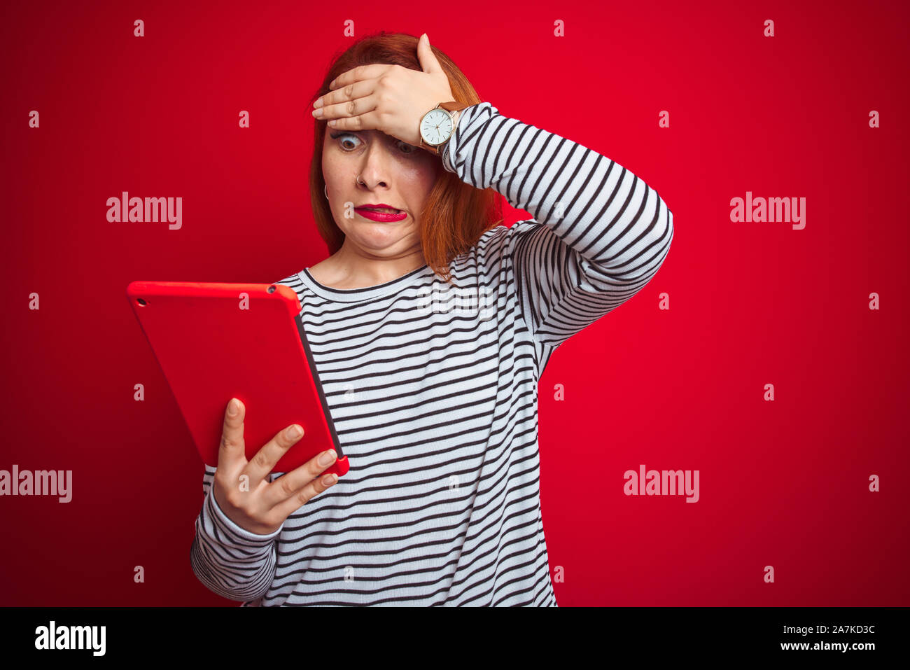 Young beautiful redhead woman using tablet over red isolated background ...