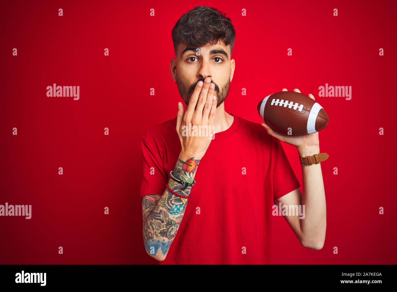 Young athlete man with tattoo holding football ball standing over ...