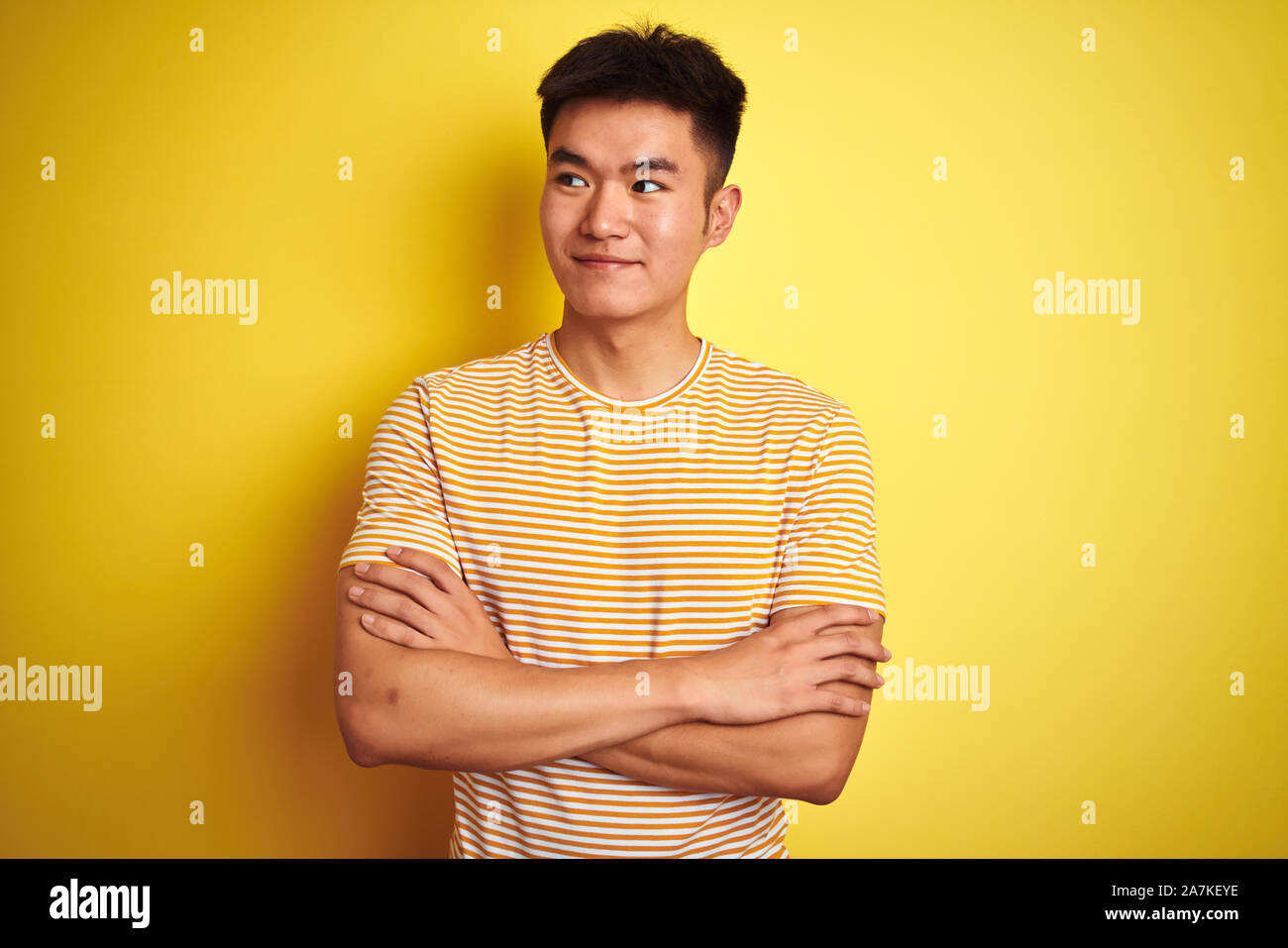 Young asian chinese man wearing t-shirt standing over isolated yellow ...