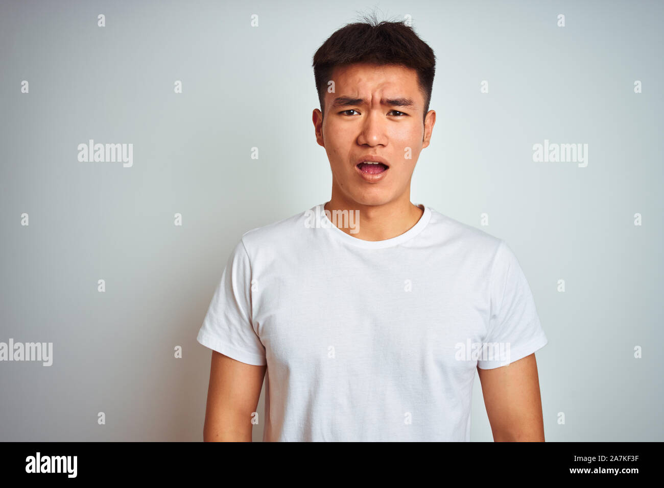 Young asian chinese man wearing t-shirt standing over isolated white ...