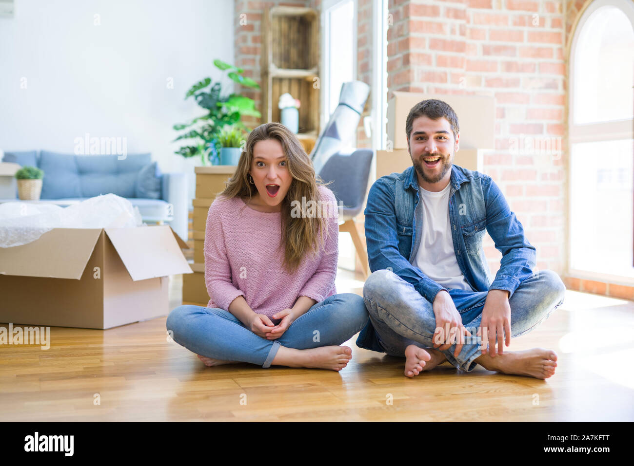 Young beautiful couple moving to a new house sitting on the floor ...