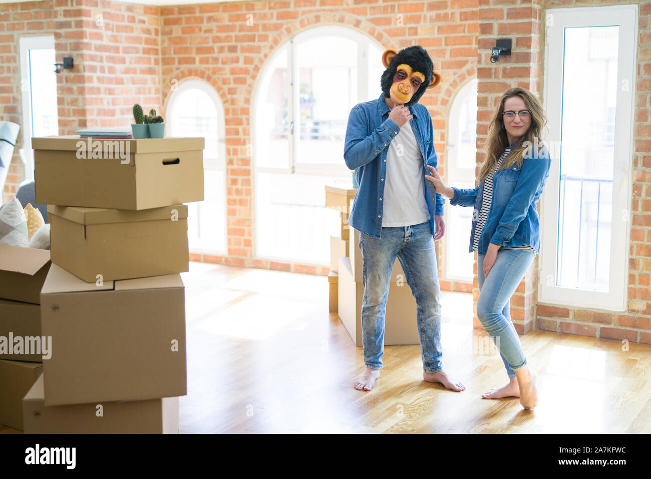 Young couple having fun wearing a monkey mask moving to a new apartment ...
