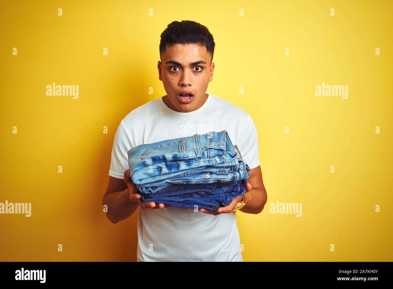 Young brazilian shopkeeper man holding jeans standing over isolated ...