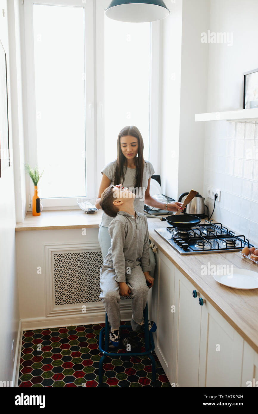 Cute little boy and his mom smiling and cooking in kitchen at home ...