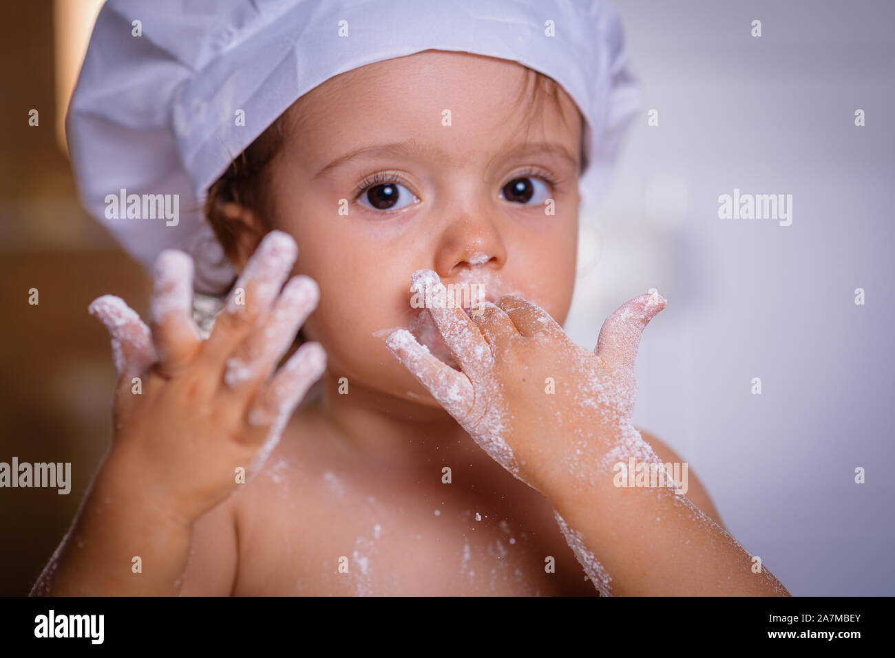A sweet small chef cook in a white culinary cap the eating flour from ...