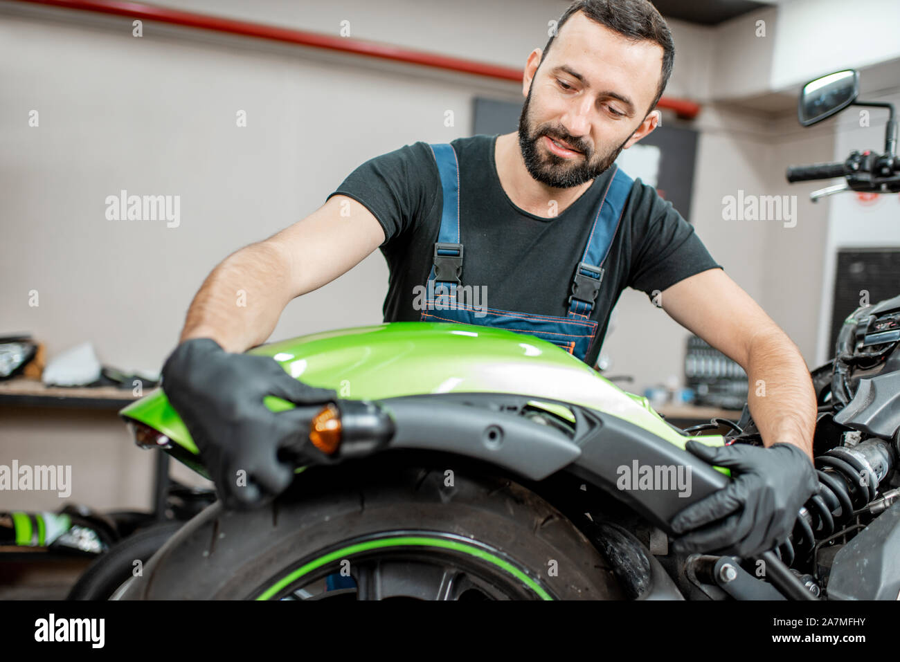 Handsome worker in overalls mounting motorcycle wing after a repairment ...