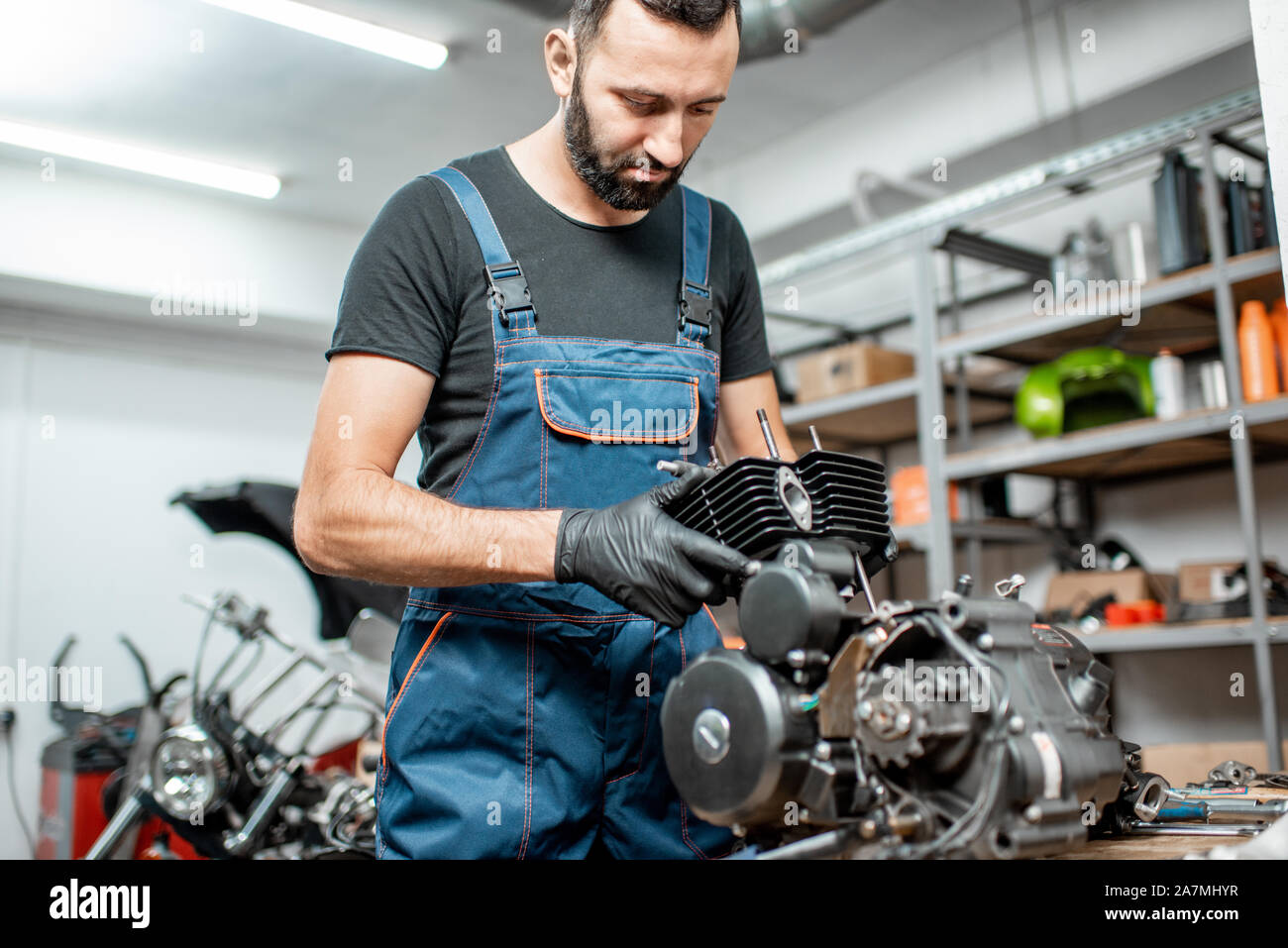 Workman in overalls disassembling motorcycle engine during a repairment ...
