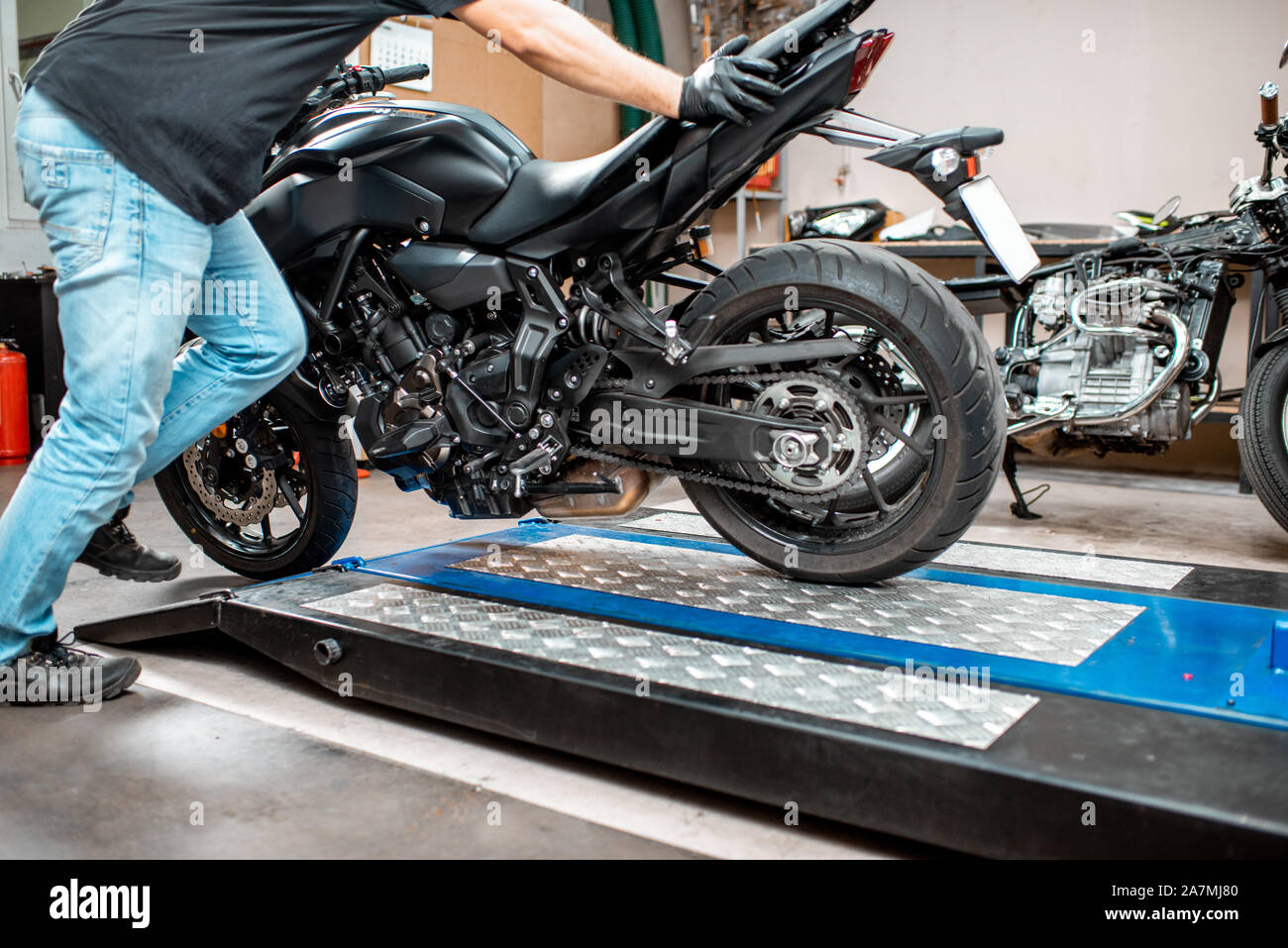 Worker putting motorcycle on a lift, preparing for the repairment in ...
